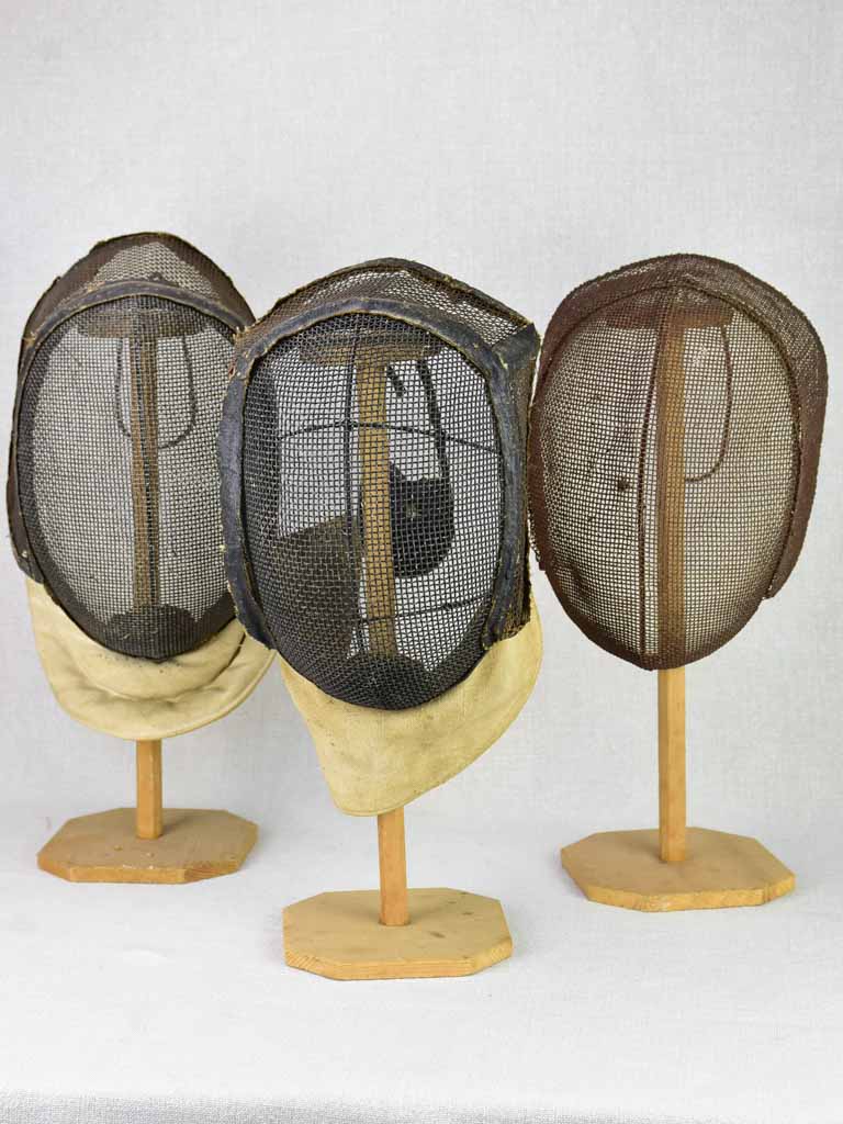 Collection of three antique French fencing masks on vintage hat stands